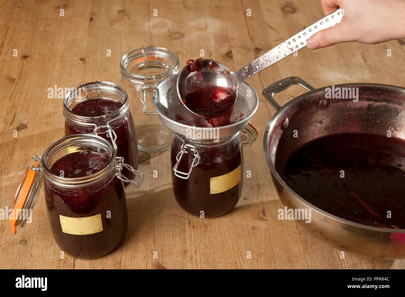 Spooning plum and cinnamon jam into sterilized jars, using ladle and ...