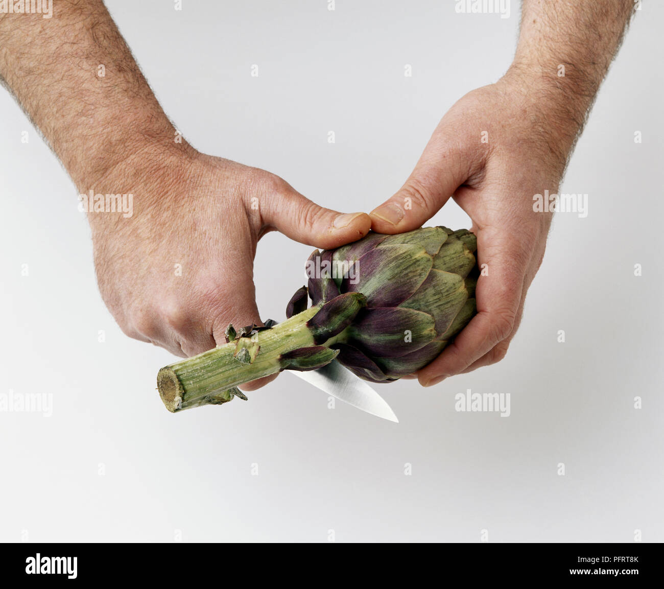 Cutting stalk off of artichoke head, using a sharp knife, close-up ...