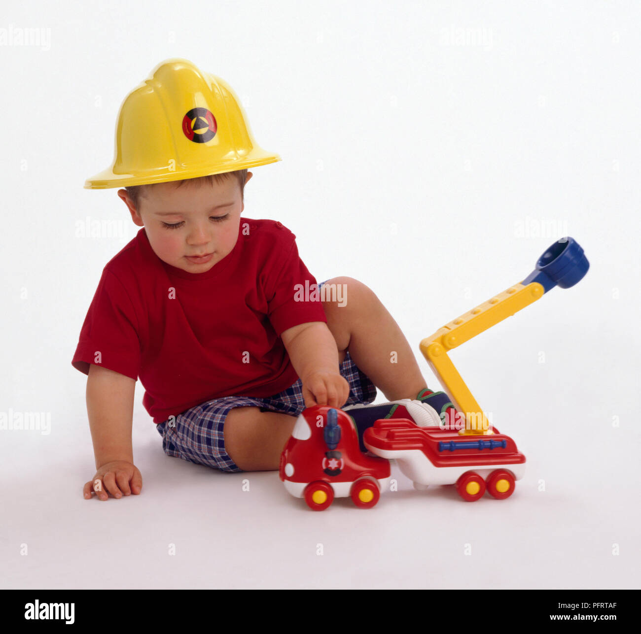 Toddler wearing yellow firefighter's helmet and playing with toy fire ...