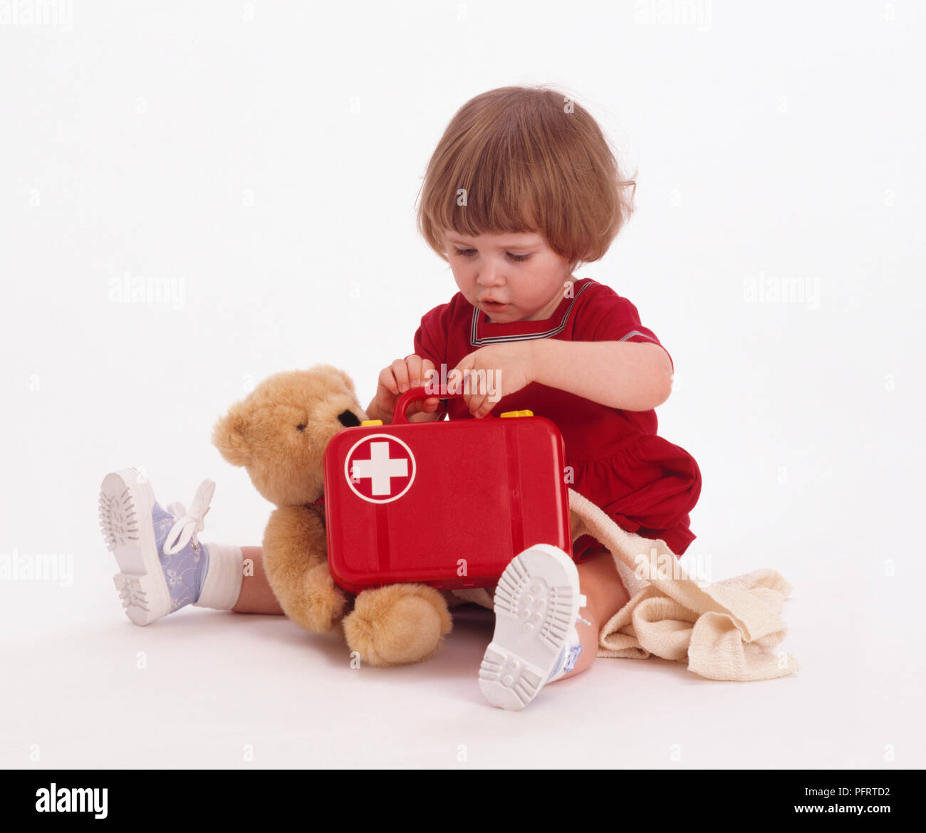 Toddler sitting on floor holding toy first aid box an teddy bear Stock ...