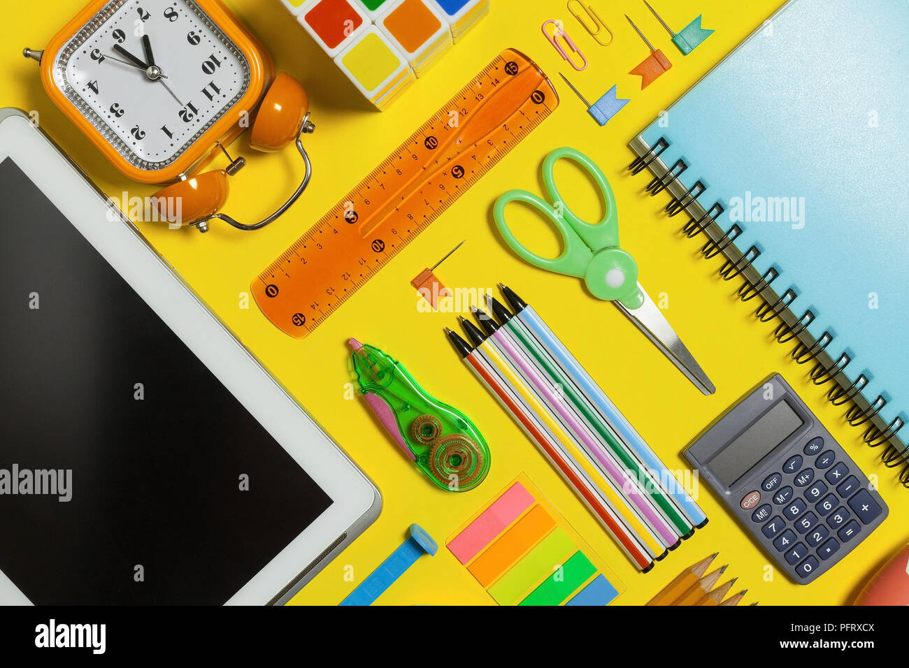 different school and office stationary and gadgets lying on a yellow ...