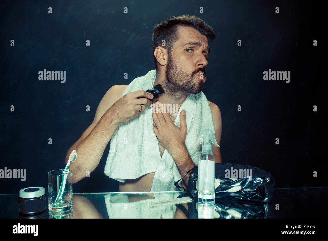 The young man in bedroom sitting in front of the mirror scratching his ...