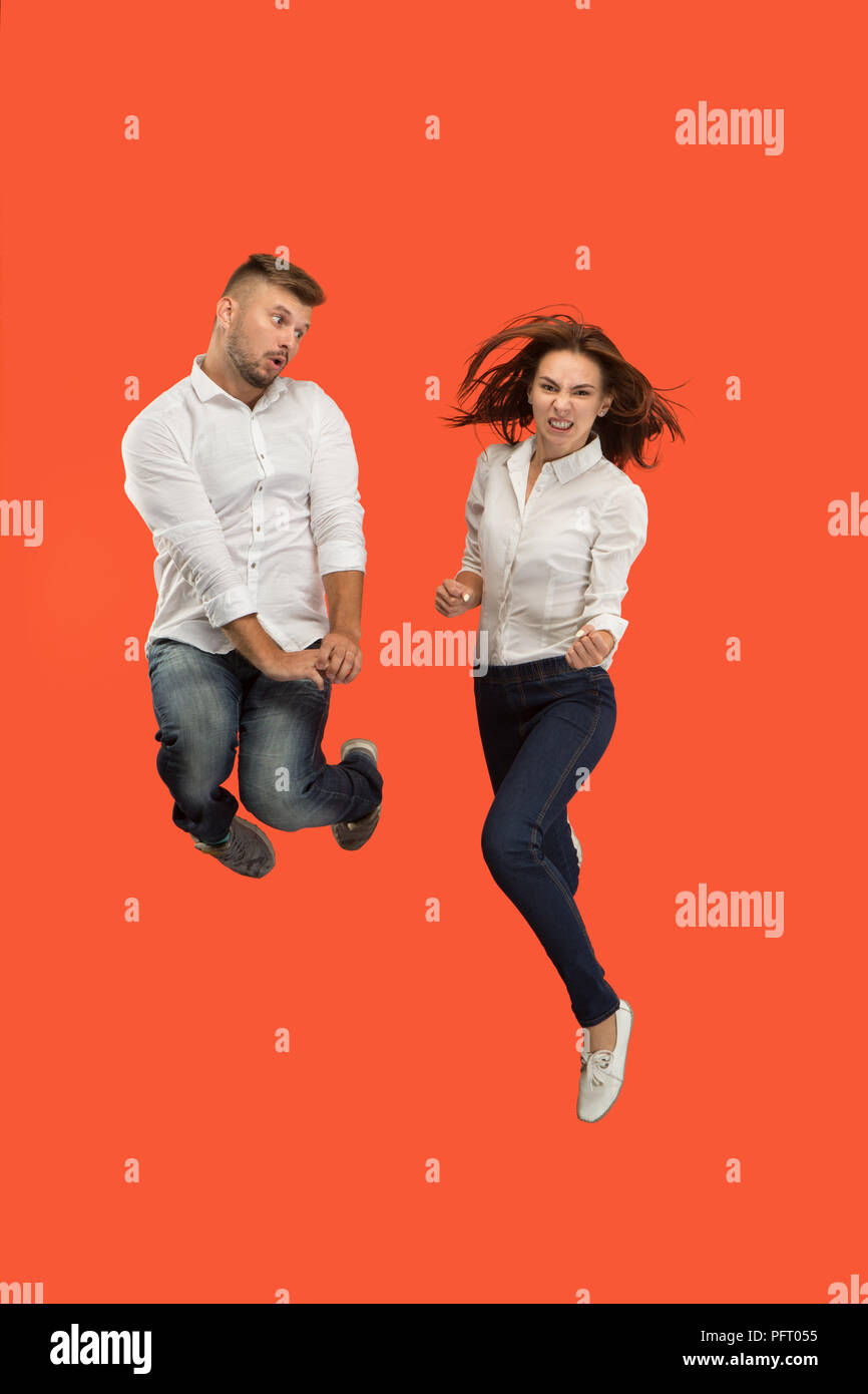 The man and angry woman jumping against red studio background. Runnin ...