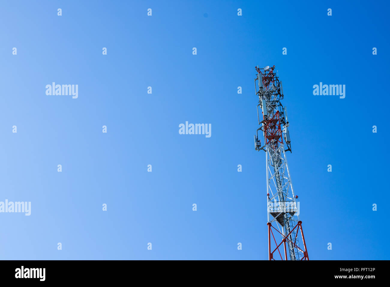 Red and white tower of communications with with a lot of different antennas under clear sky ...