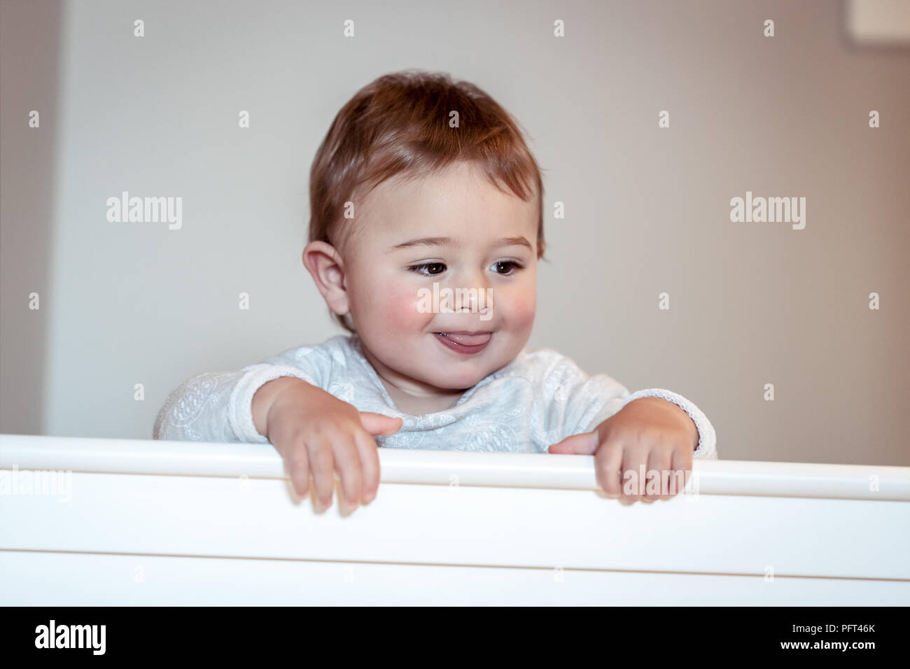 Sweet baby boy standing in his nice white cot, little child in ...