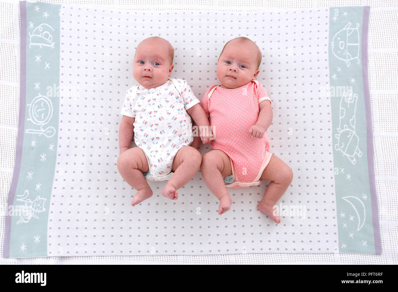 Twin 13-week old girls lying side by side on a blanket, facing upwards ...
