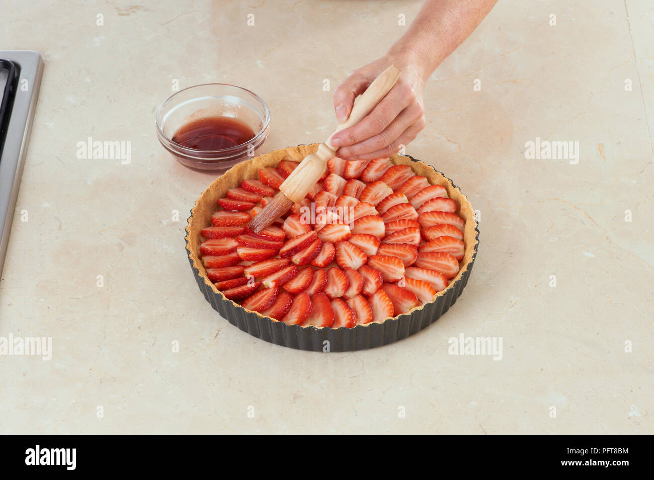 Person using basting brush to apply glaze to strawberries in shortcrust ...