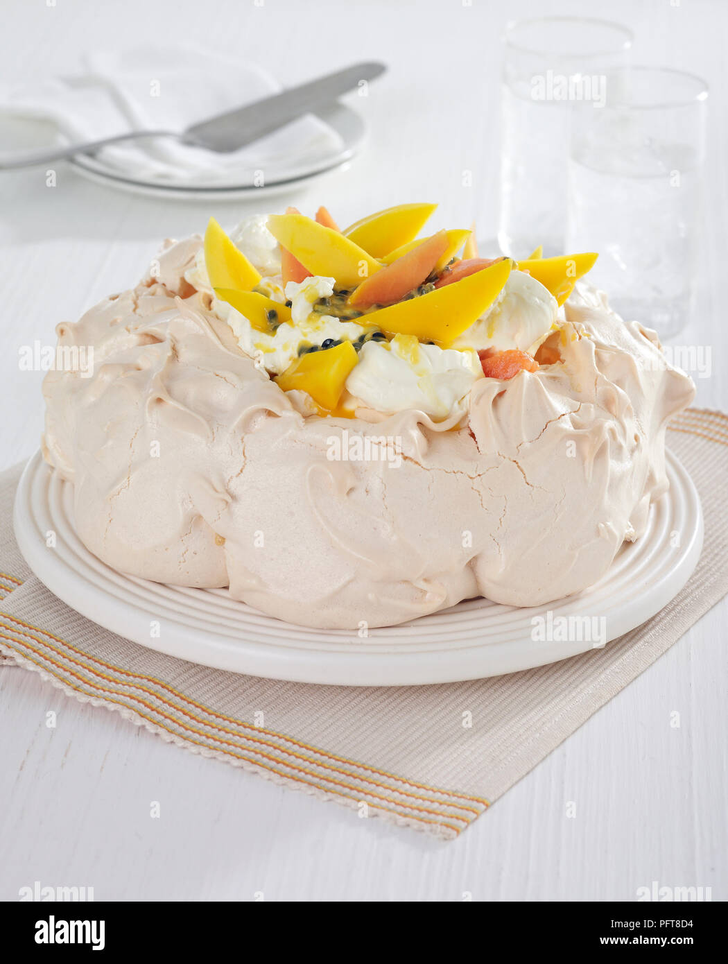 Pavlova topped with tropical fruit and cream served with glasses of ...