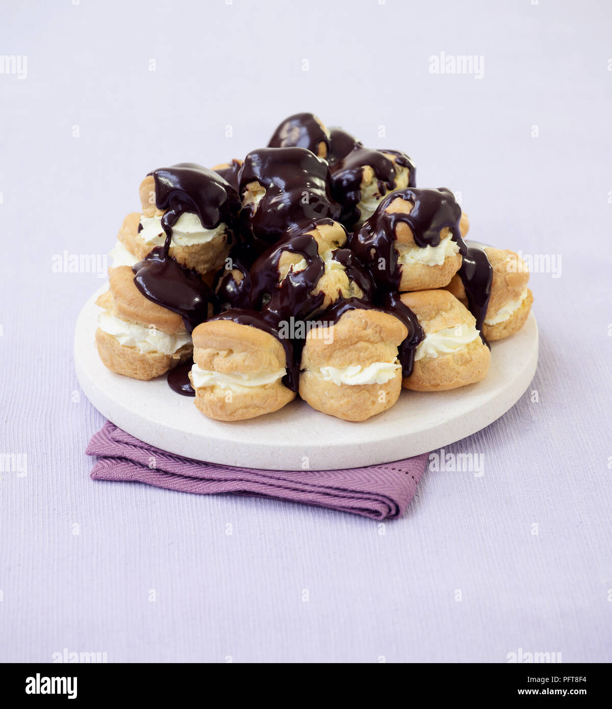 Stack of profiteroles and whipped cream coated with chocolate on marble ...
