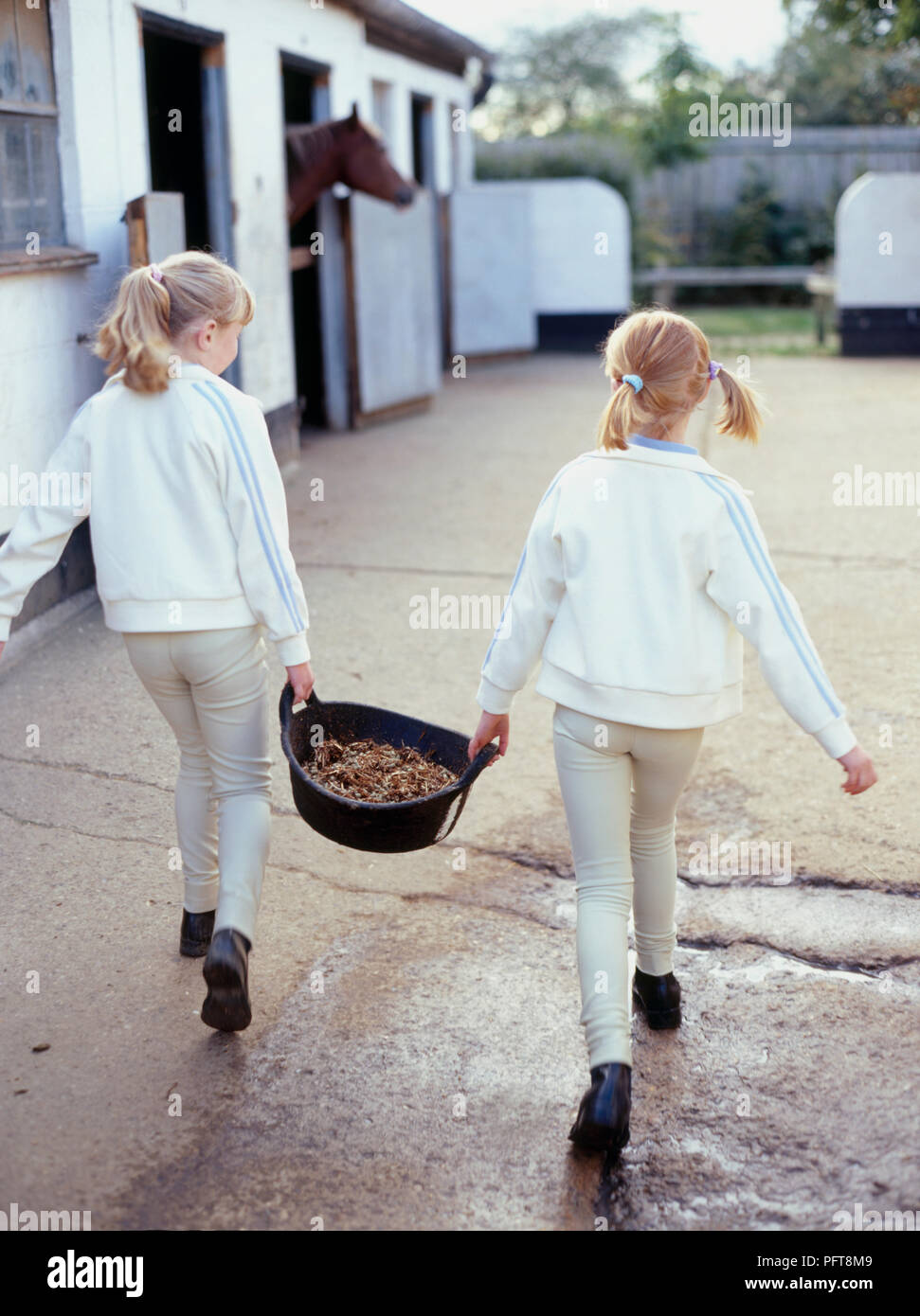 Two young girls carrying bucket of food to feed pony in stable Stock ...