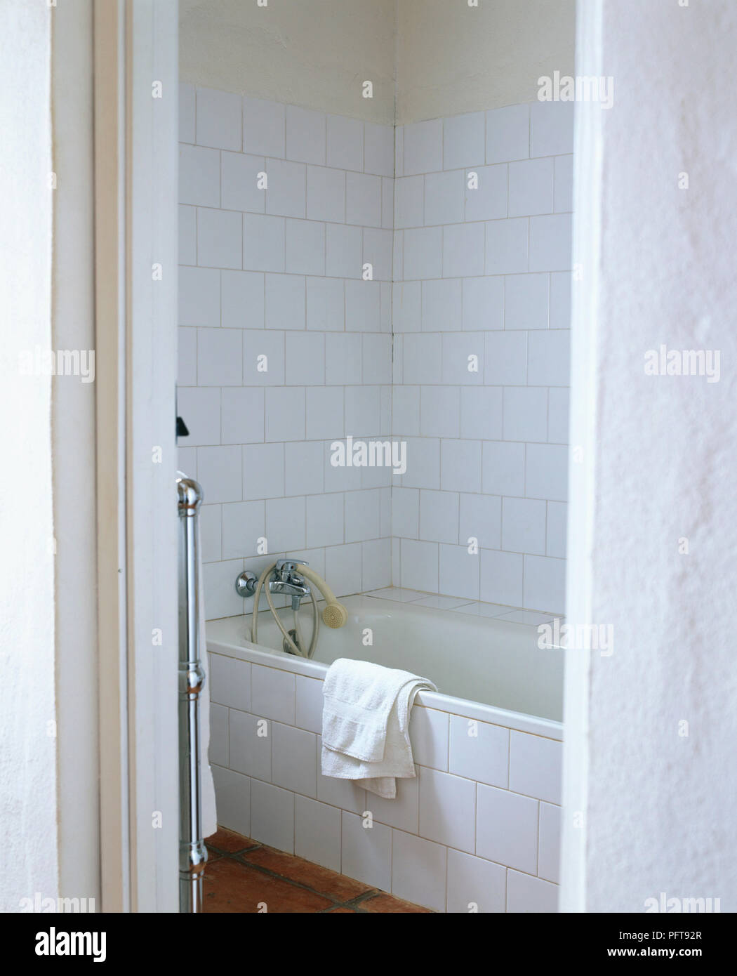 White towel on side of bath in tiled bathroom seen through open door ...