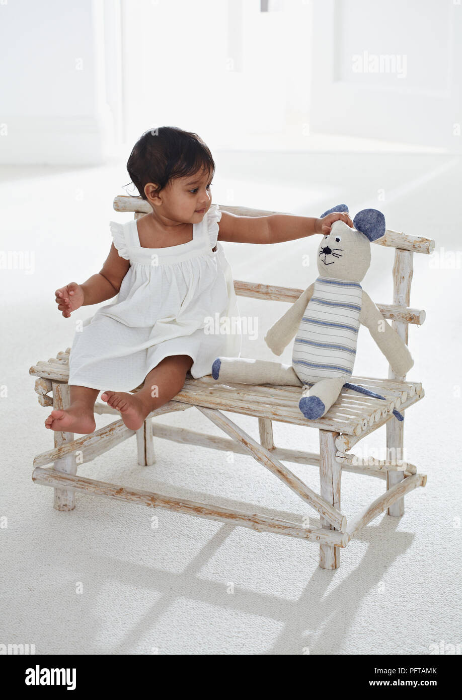 Baby girl sitting on small bench with toy mouse seated next to her, 11 ...