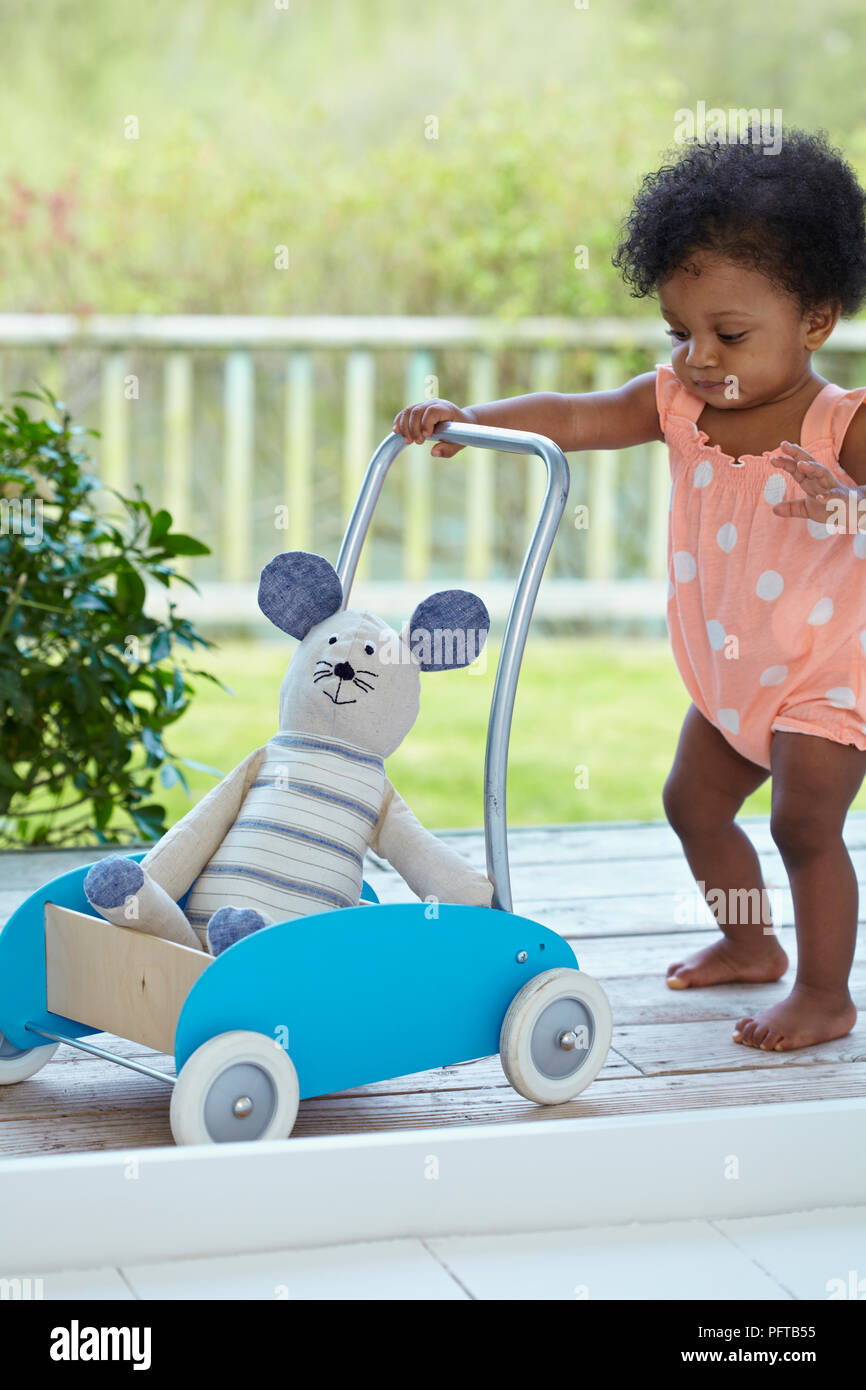 Baby girl pushing cart containing toy rabbit, 10 months Stock Photo - Alamy