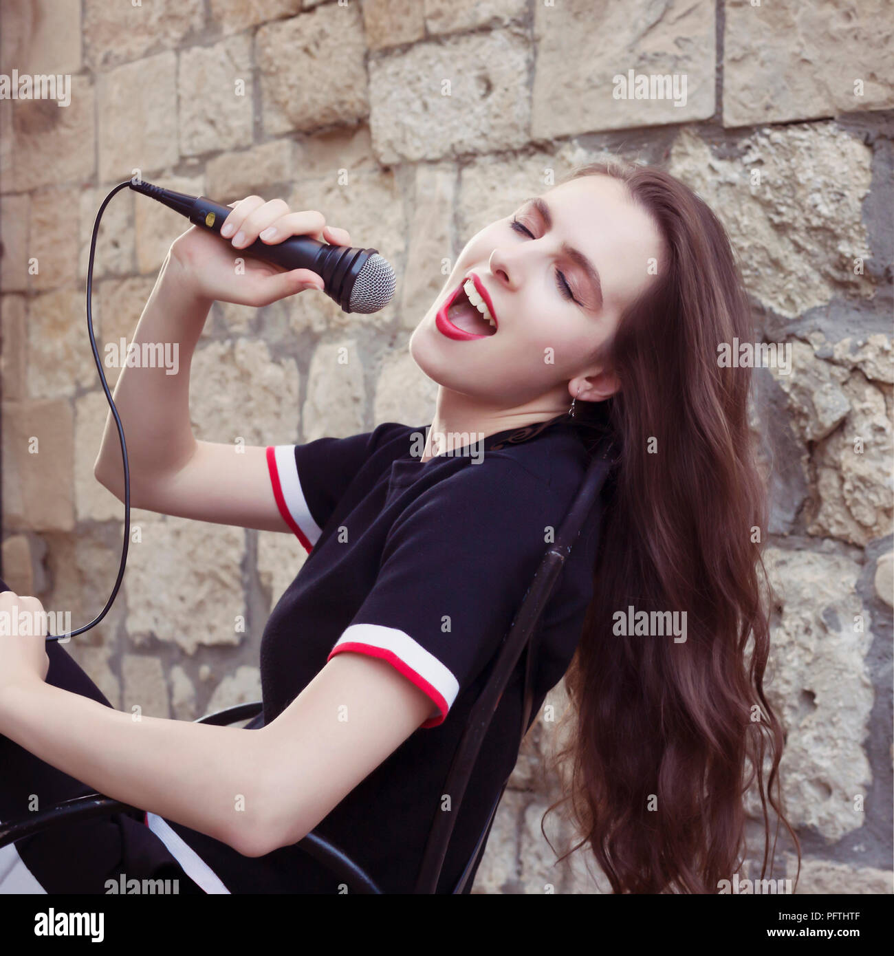 Beautiful Young Woman singing with microphone Against Rock Wall outdoor ...