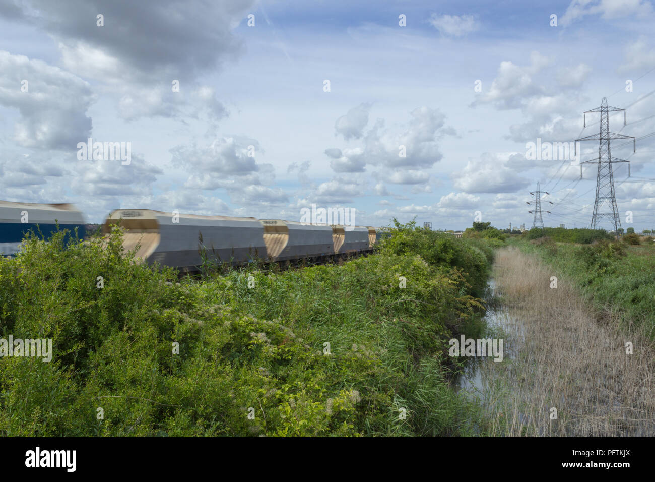 Freight train running alongside line of pylons to a distant industrial ...