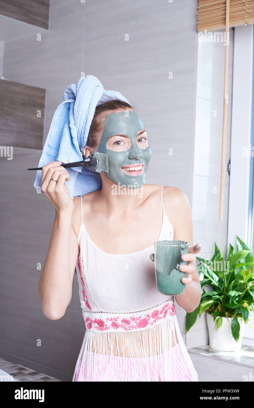 Woman applying mask moisturizing skin cream on face looking in bathroom ...