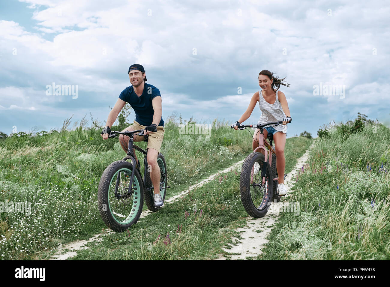 Happy couple racing on a bike along the sand and grass high in the ...