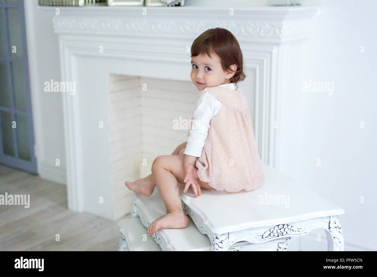 Sweet little girl at home sitting on modern chair relaxing in white living room Stock Photo - Alamy