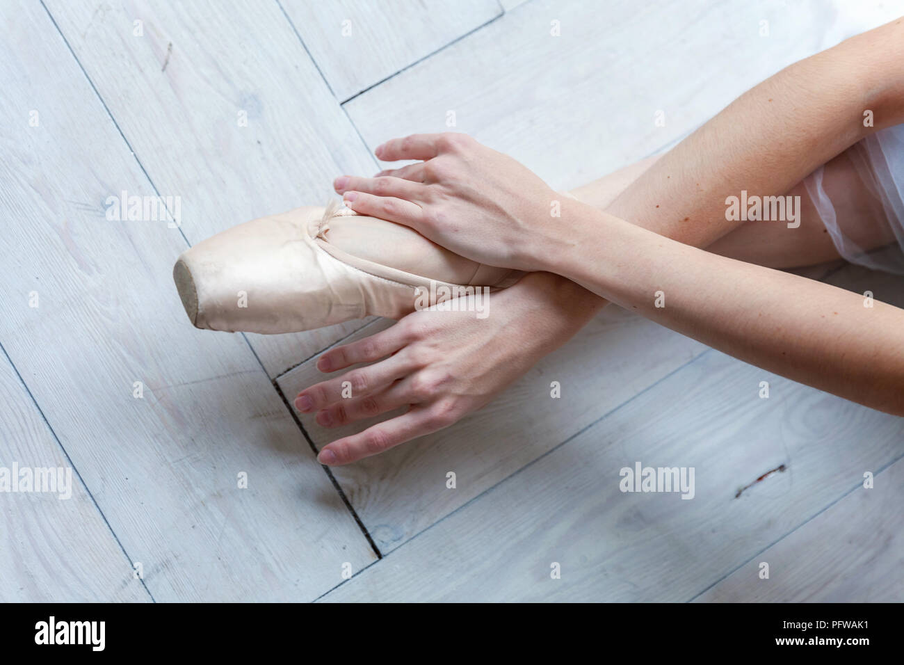 Closeup of young ballerina legs in pointe shoes at white wooden floor background, with copy ...