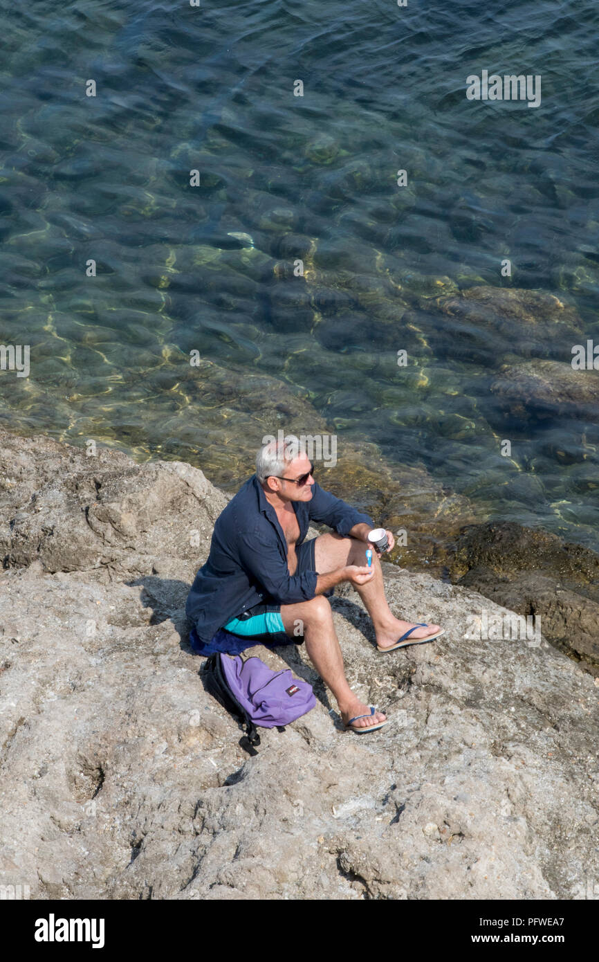 man sitting on rocks at the seaside or beach eating an ice cream from a ...