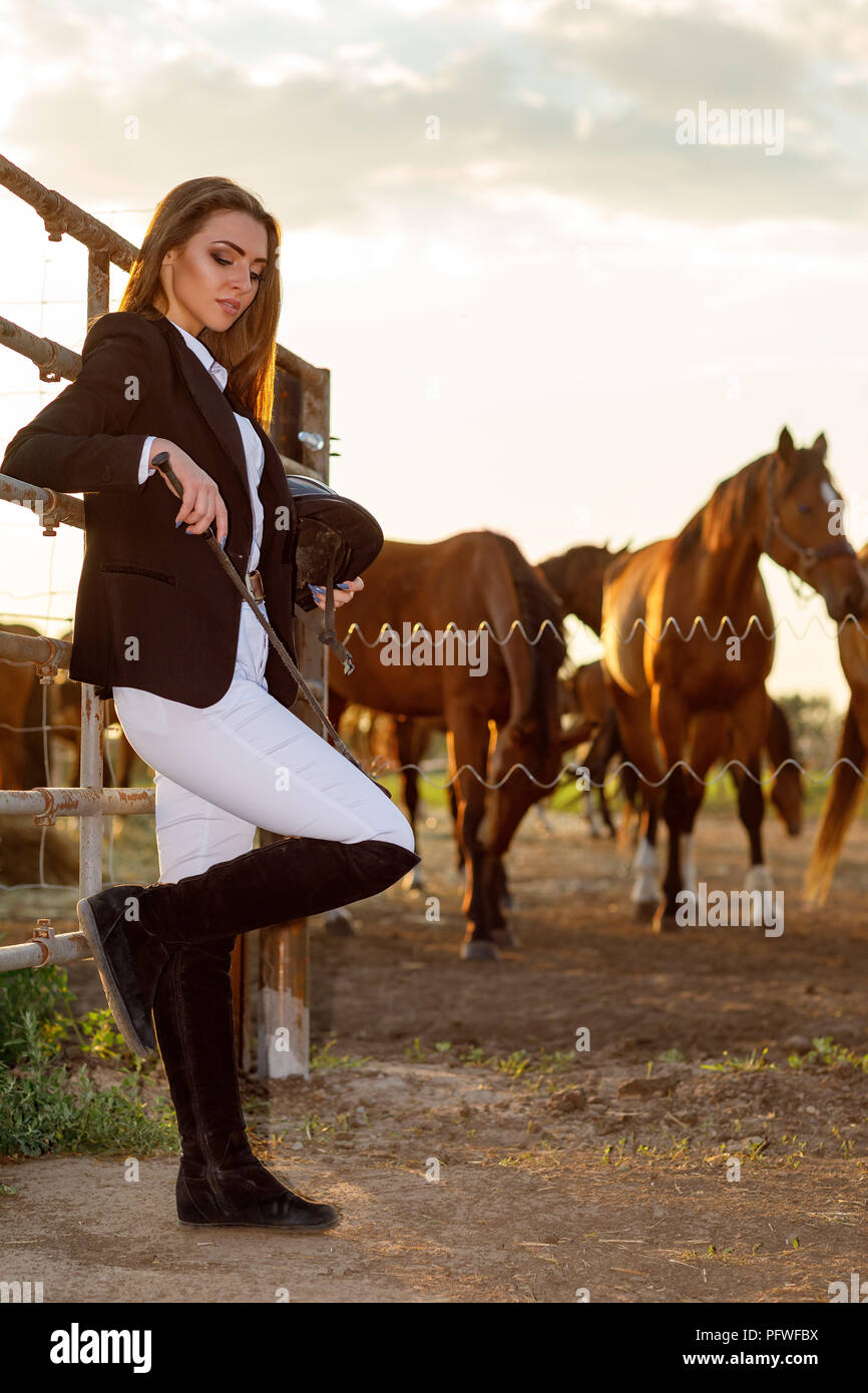 beautiful rider woman with whip stands against the backdrop of horses ...