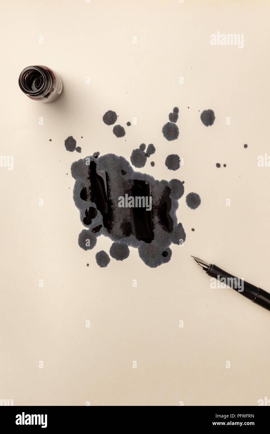 An overhead photo of an ink well with drops of ink and a nib pen, with ...