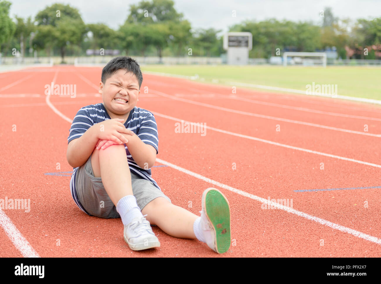 Obese boy feeling pain after having his knee injured on the track ...