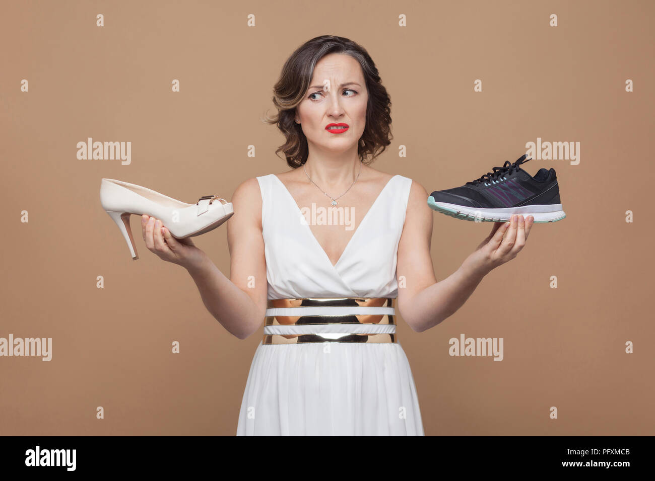 Anger woman in white dress holding high heels and sneakers and looking ...
