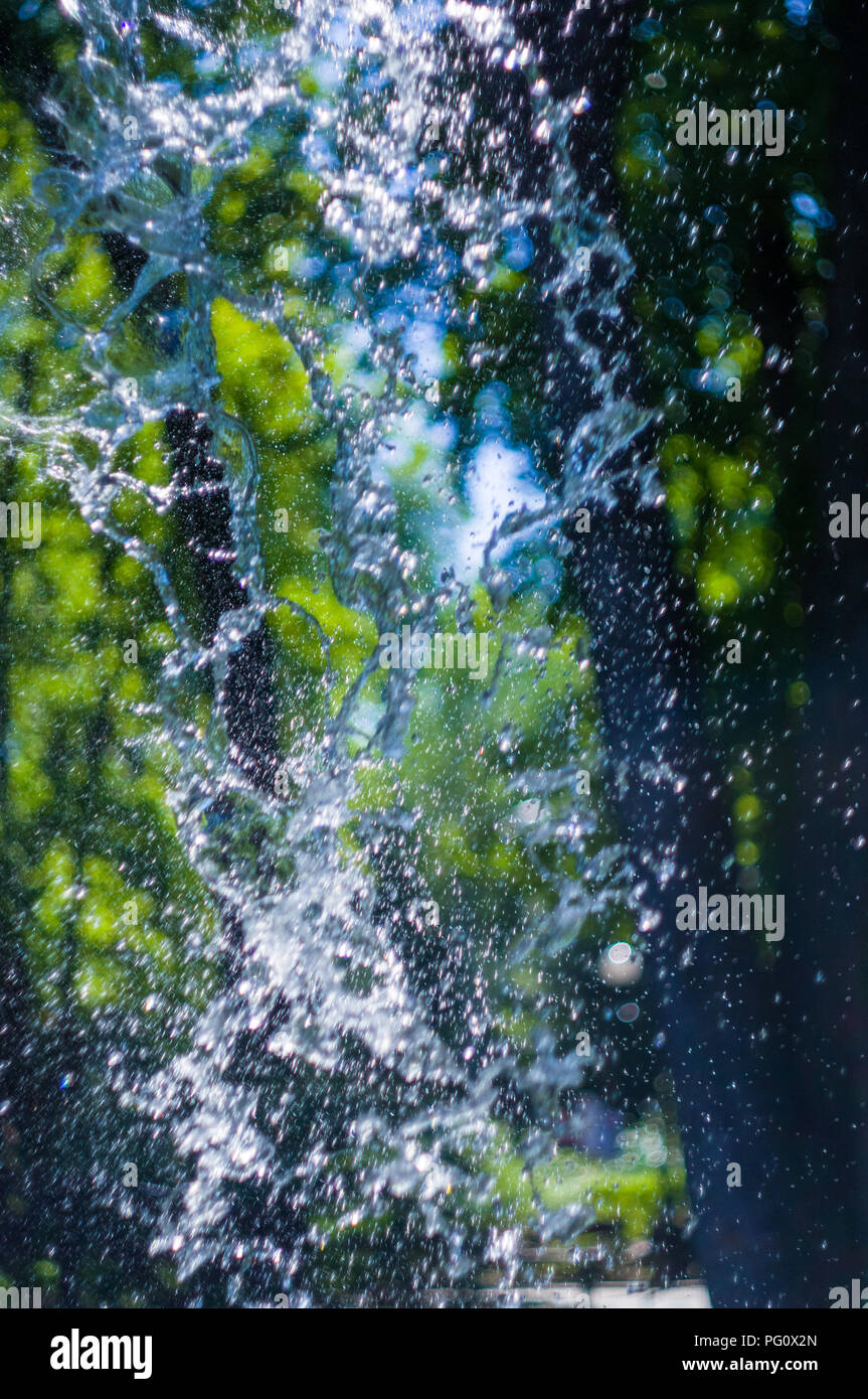 transparent falling water vertical flows against a blue sky and green ...