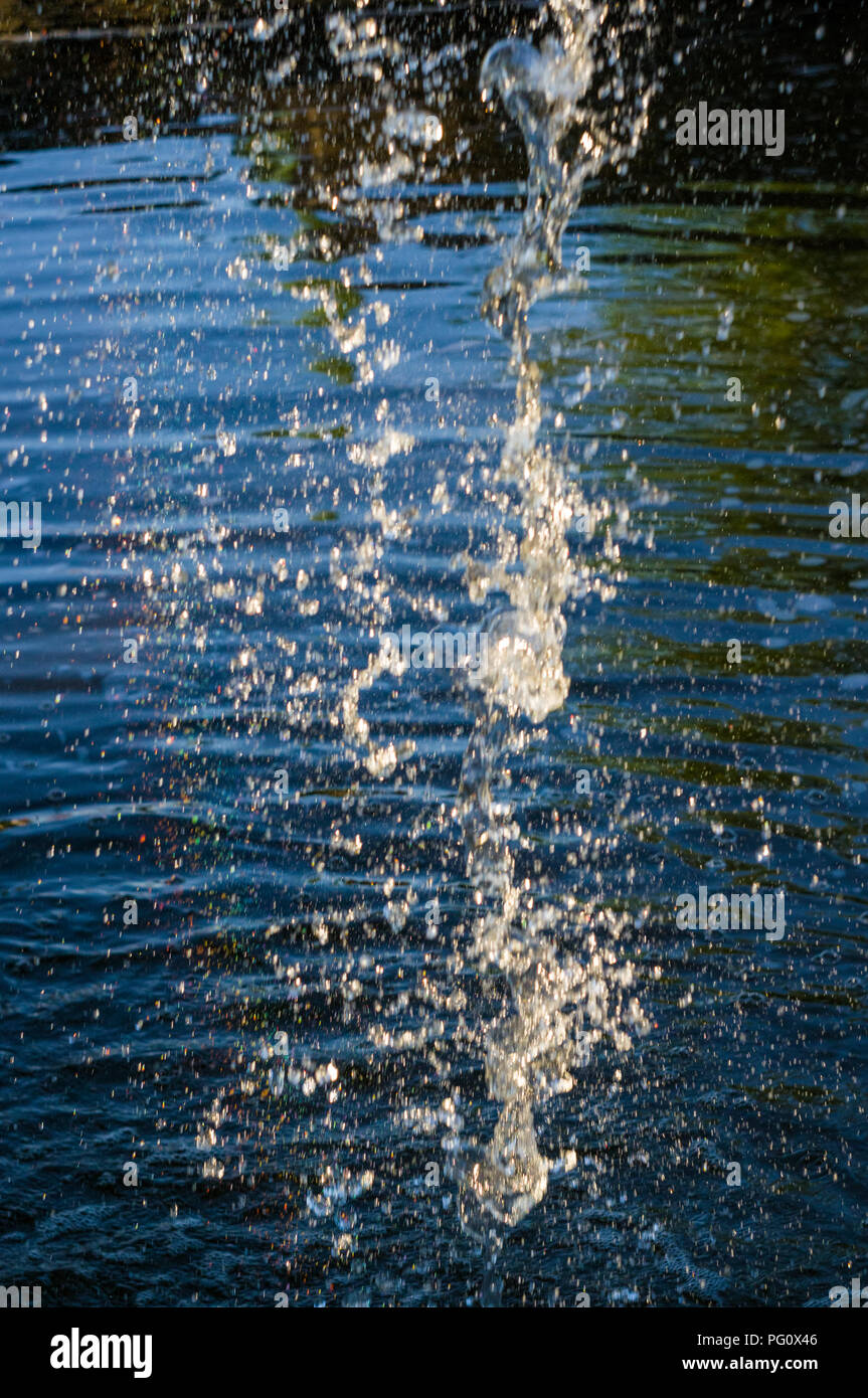 transparent falling water vertical flows against a blue sky and green ...