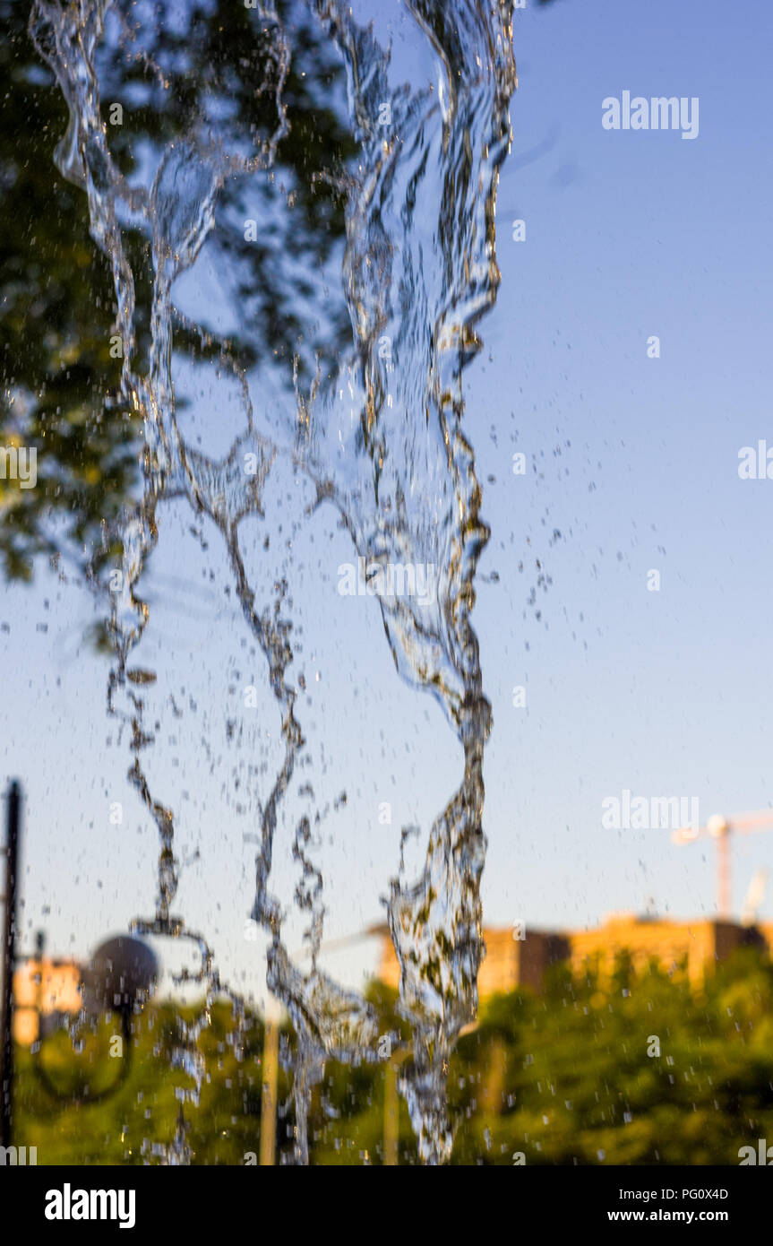 transparent falling water vertical flows against a blue sky and green ...