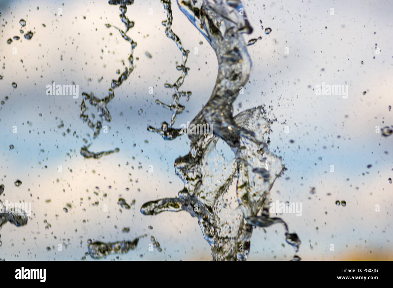 transparent falling water vertical flows against a blue sky and green ...