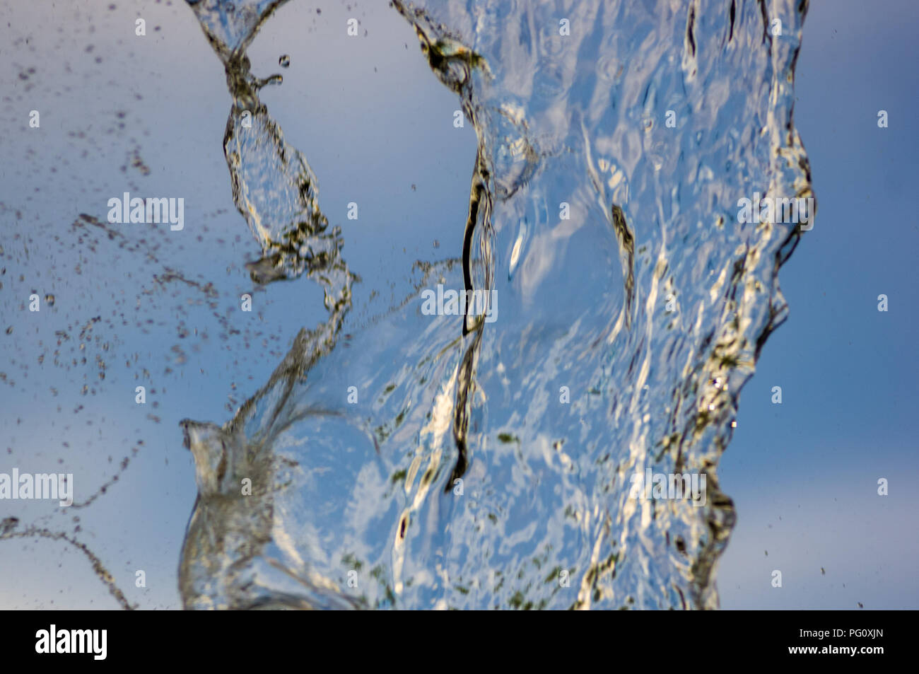 transparent falling water vertical flows against a blue sky and green ...