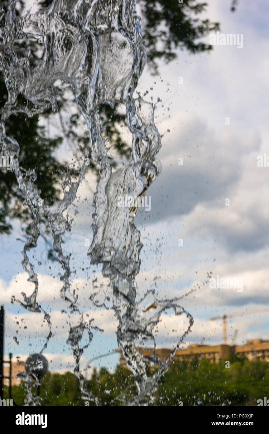 transparent falling water vertical flows against a blue sky and green ...