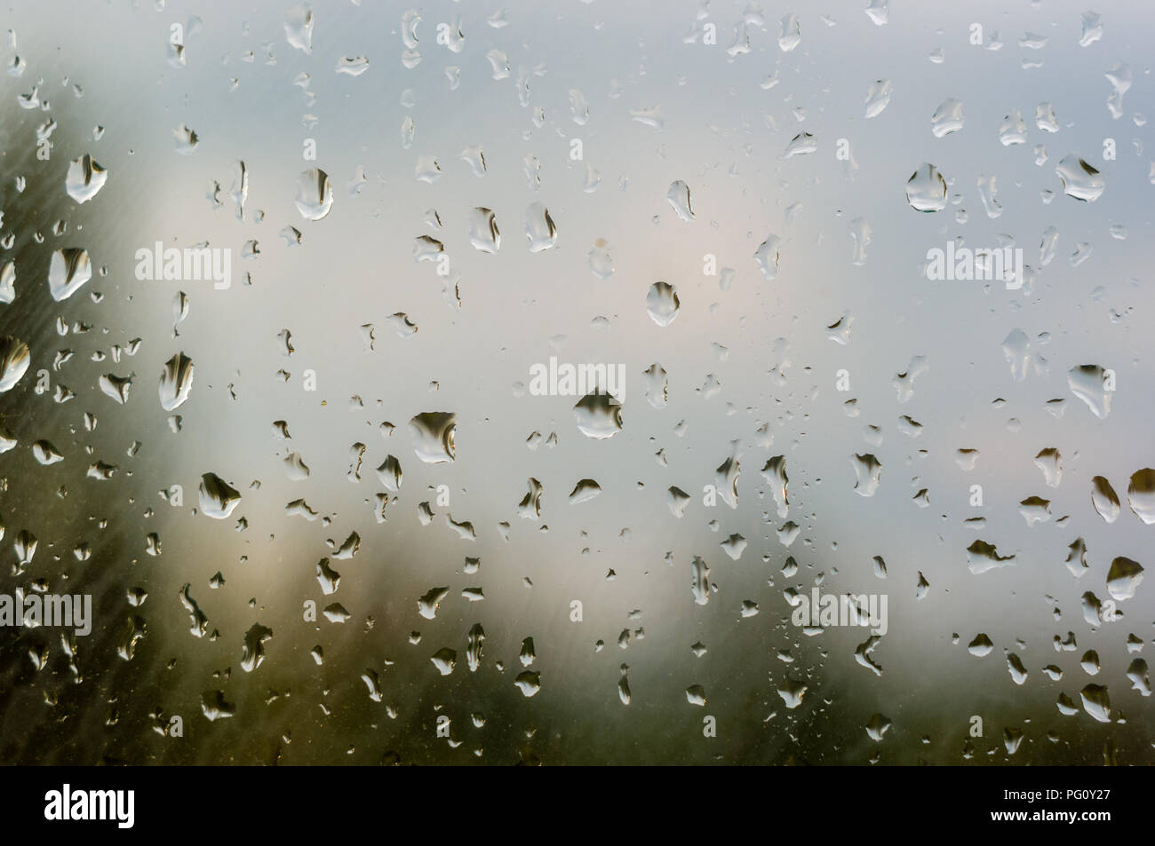 raindrops on window glass on background of cloudy sky and landscape ...