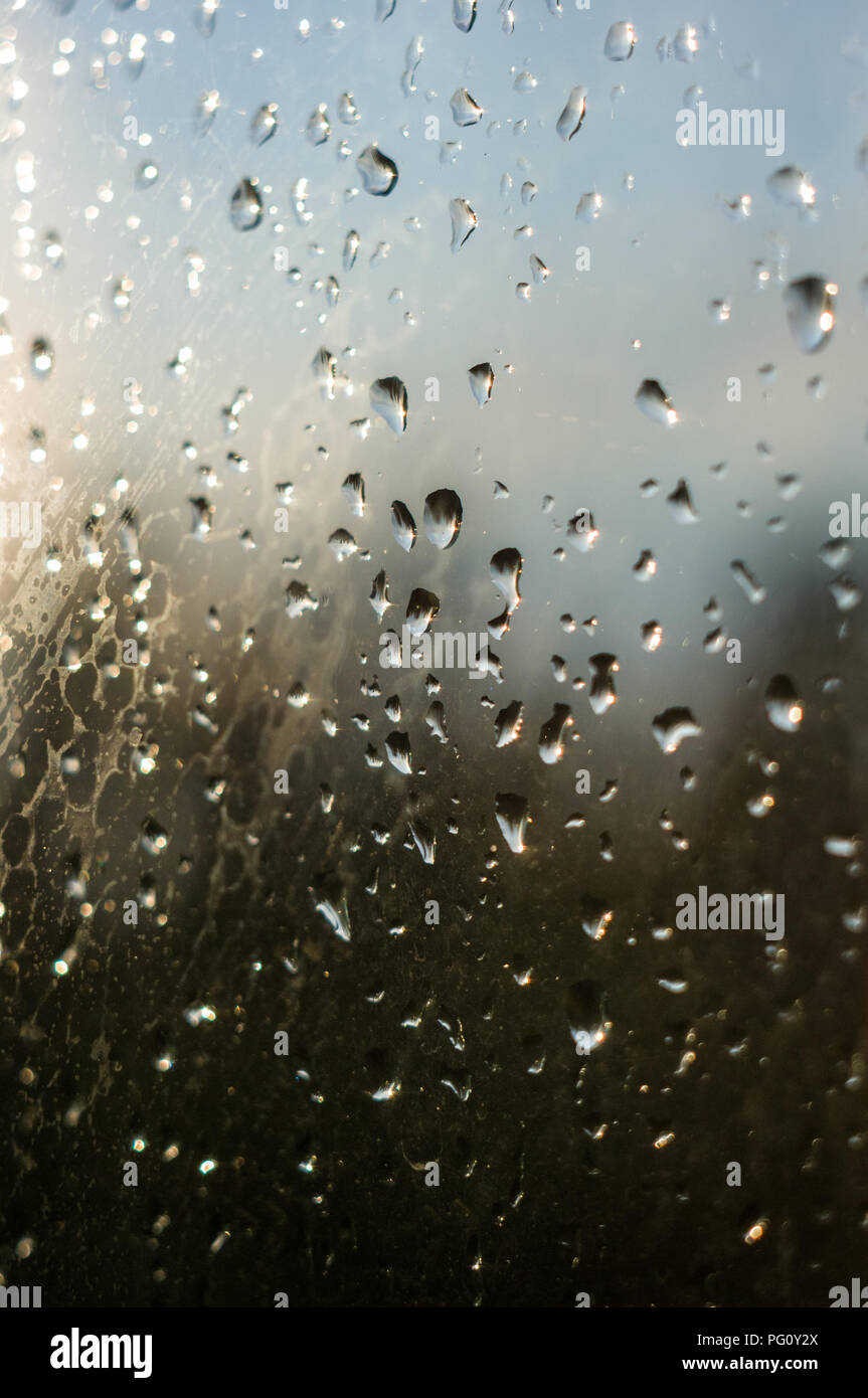 raindrops on window glass on background of cloudy sky and landscape ...