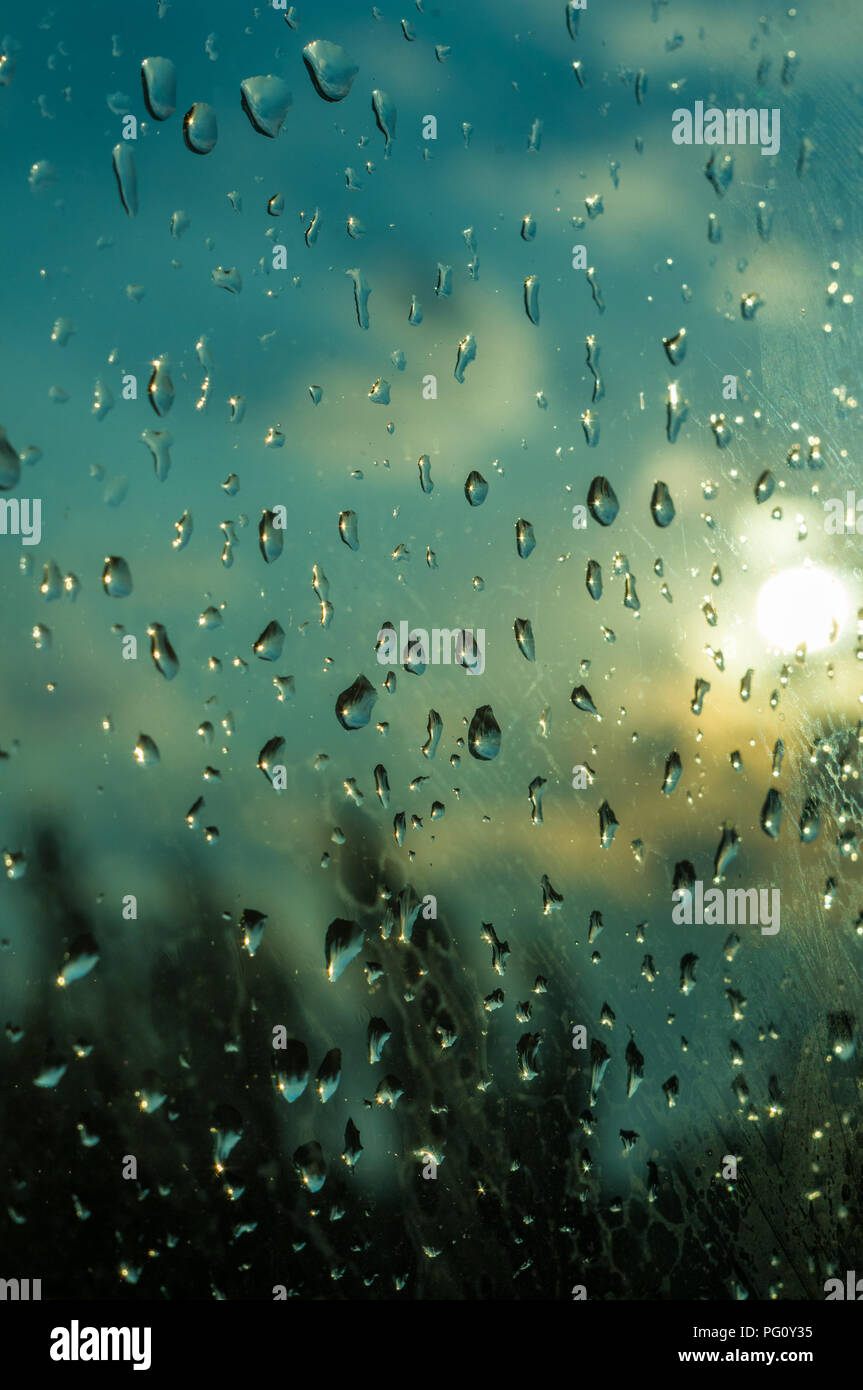 raindrops on window glass on background of cloudy sky and landscape ...