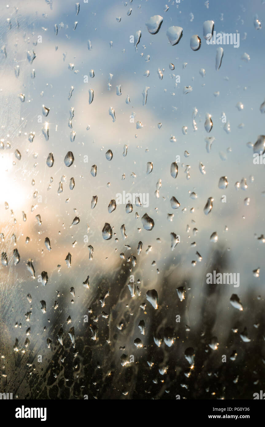 raindrops on window glass on background of cloudy sky and landscape ...