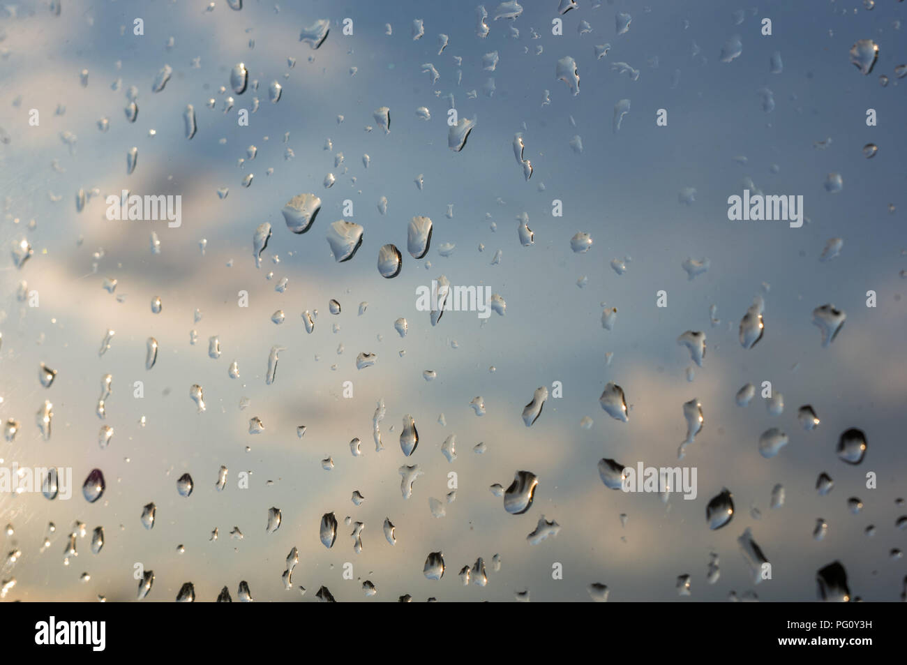 raindrops on window glass on background of cloudy sky and landscape ...