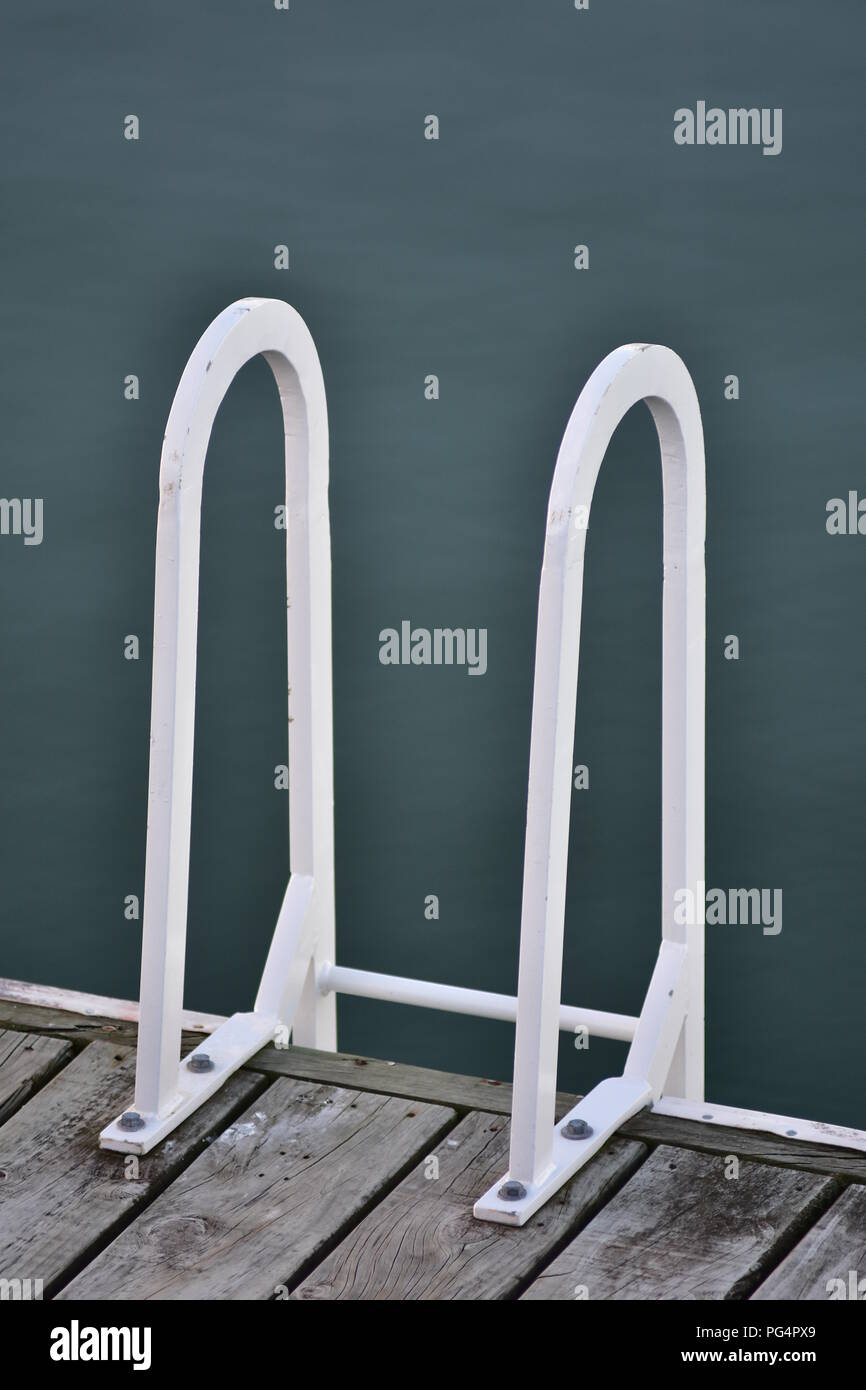White metal ladder with railing bolted to slate floor of jetty with ...