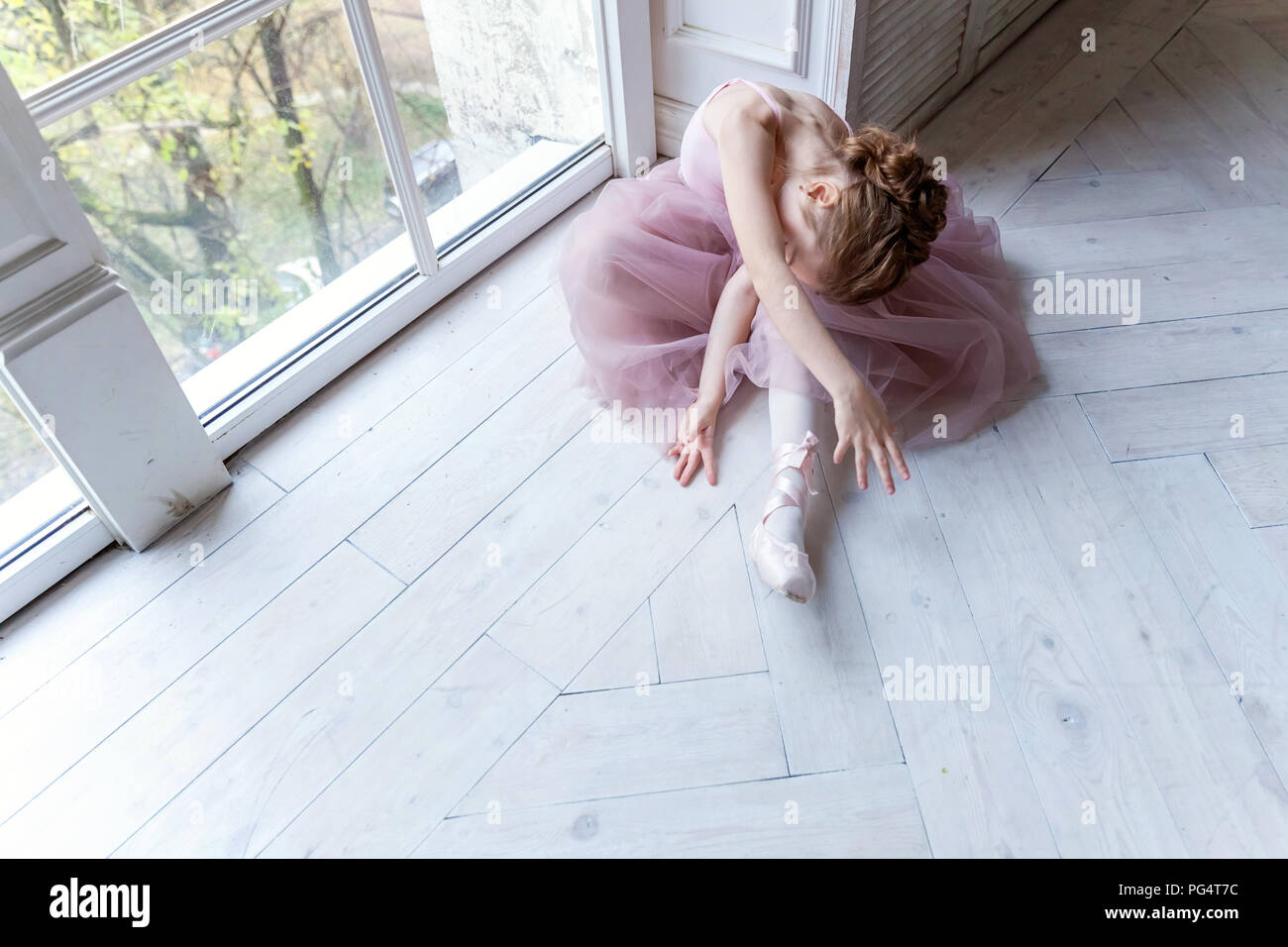 Closeup of young ballerina sit in pointe shoes at white wooden floor ...