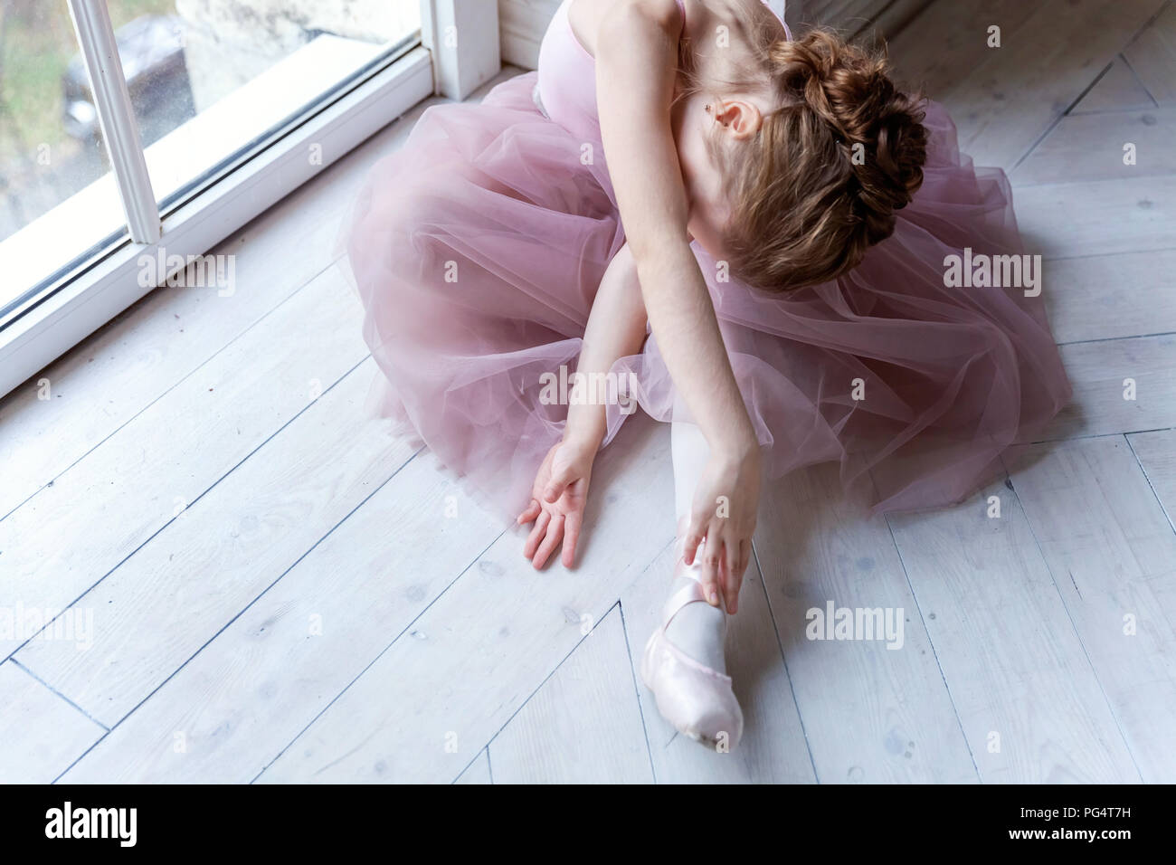 Closeup of young ballerina sit in pointe shoes at white wooden floor ...