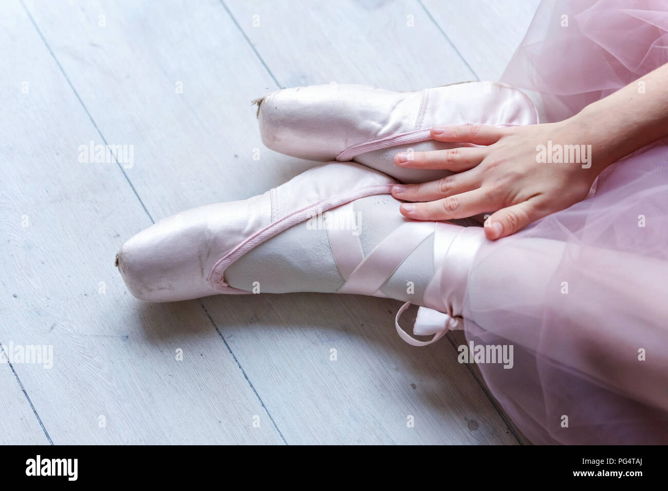 Closeup of young ballerina legs in pointe shoes at white wooden floor background, with copy ...