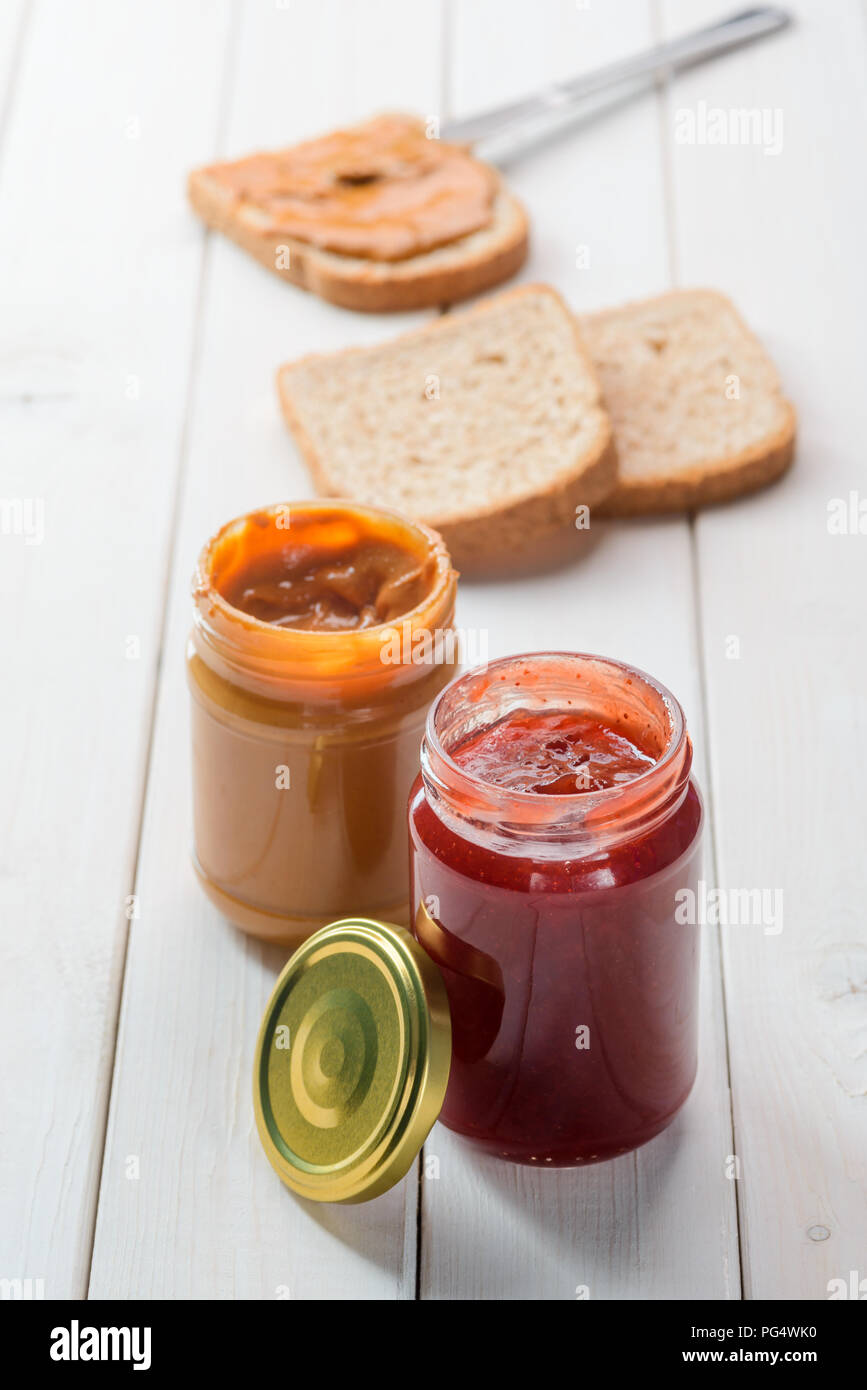 Tasty jam and peanut butter jars, close-up. Light wooden surface ...