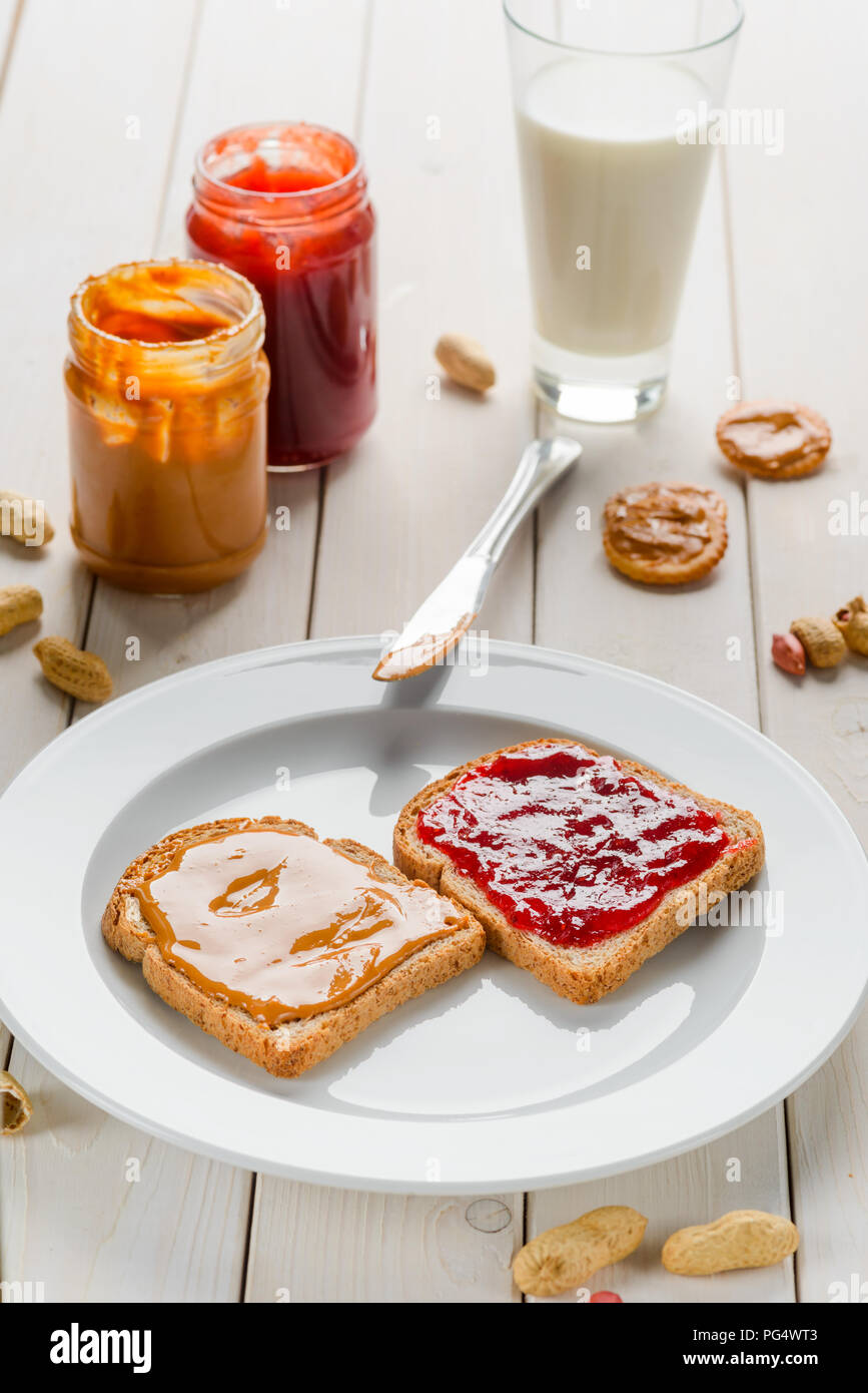 Delicious sandwich, glass of milk, jam and peanut butter jars, crackers ...
