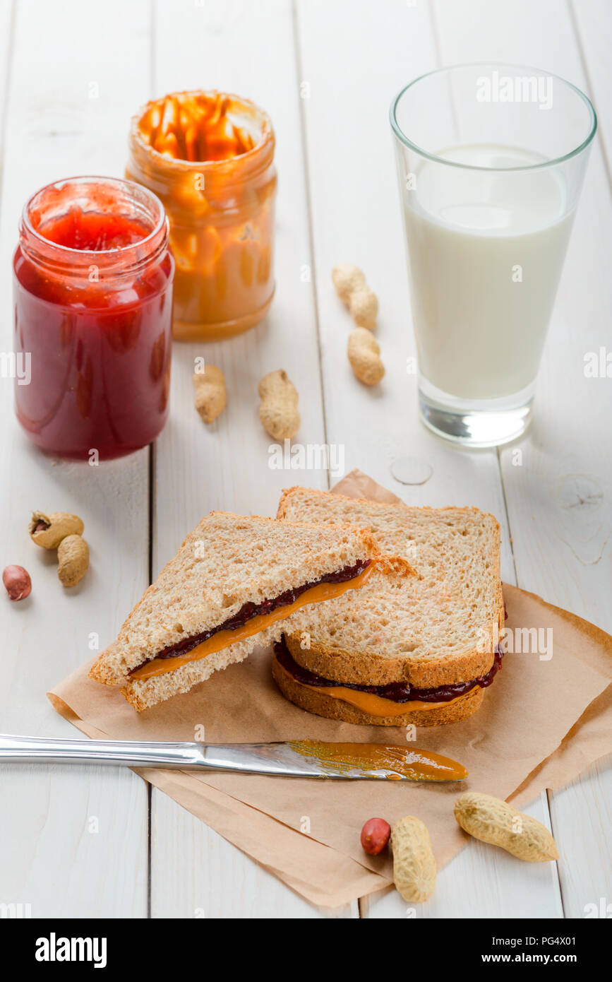 Peanuts, whole grain sandwich, jam and peanut butter jars, glass of ...