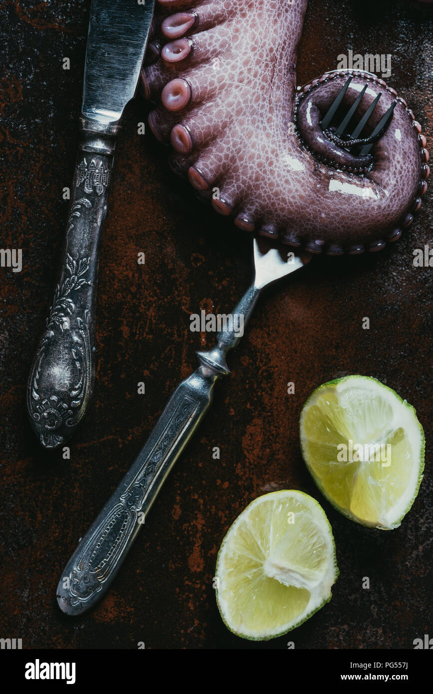 top view of big octopus tentacle with fork, knife and limes on rusty ...