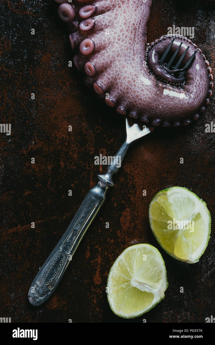 top view of big octopus tentacle with fork and limes on rusty metal ...