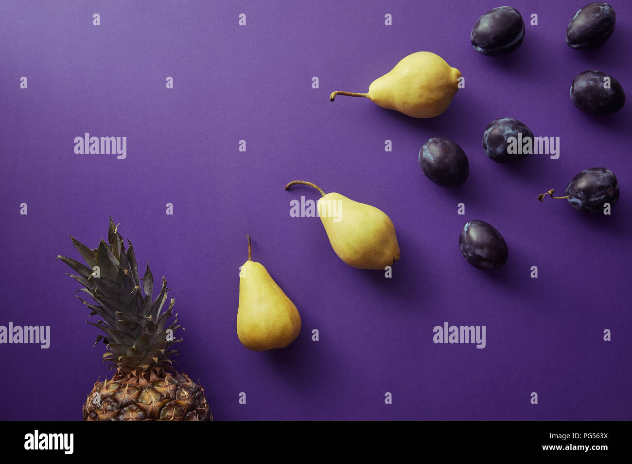 top view of pears, plums and pineapple on violet surface Stock Photo ...