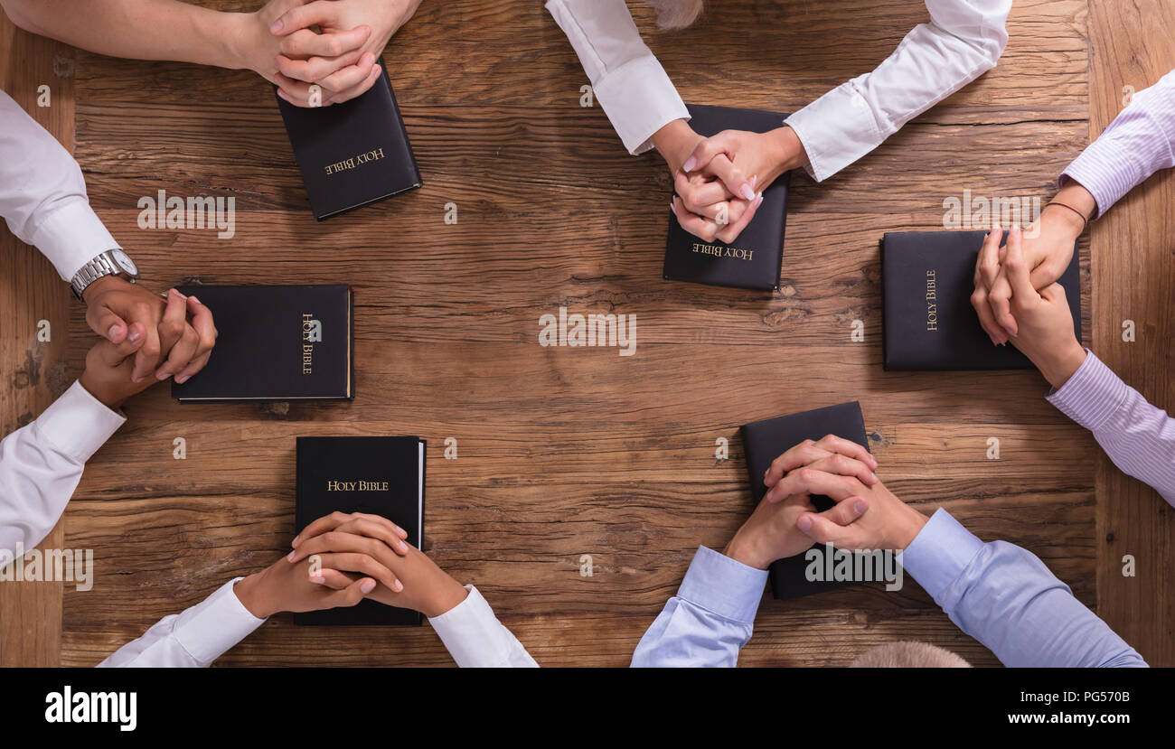 High Angle View Of People's Praying Hands On Holy Bible Stock Photo - Alamy